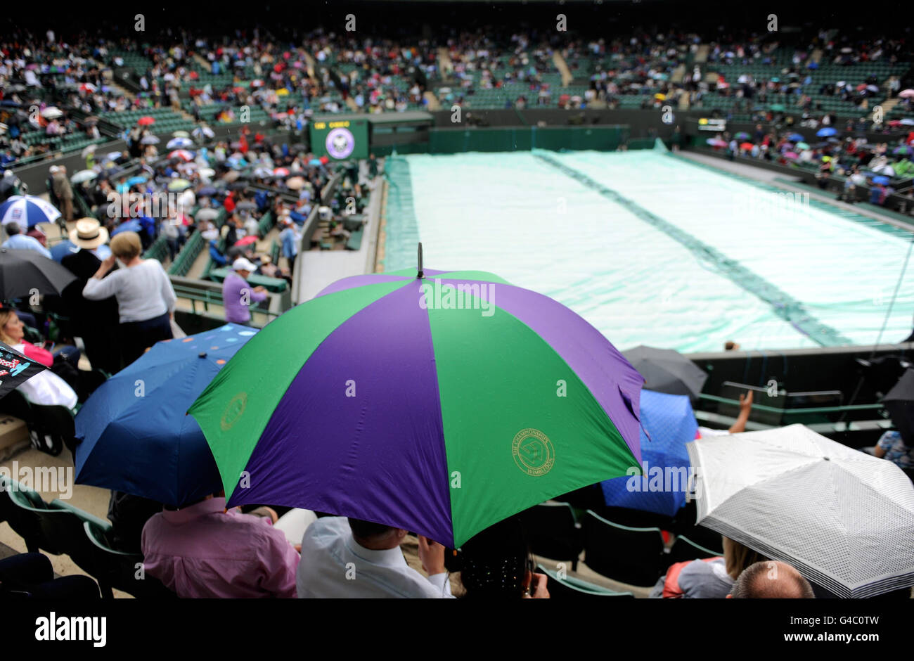 Spectators use umbrellas on Court One as the rain falls during day one ...