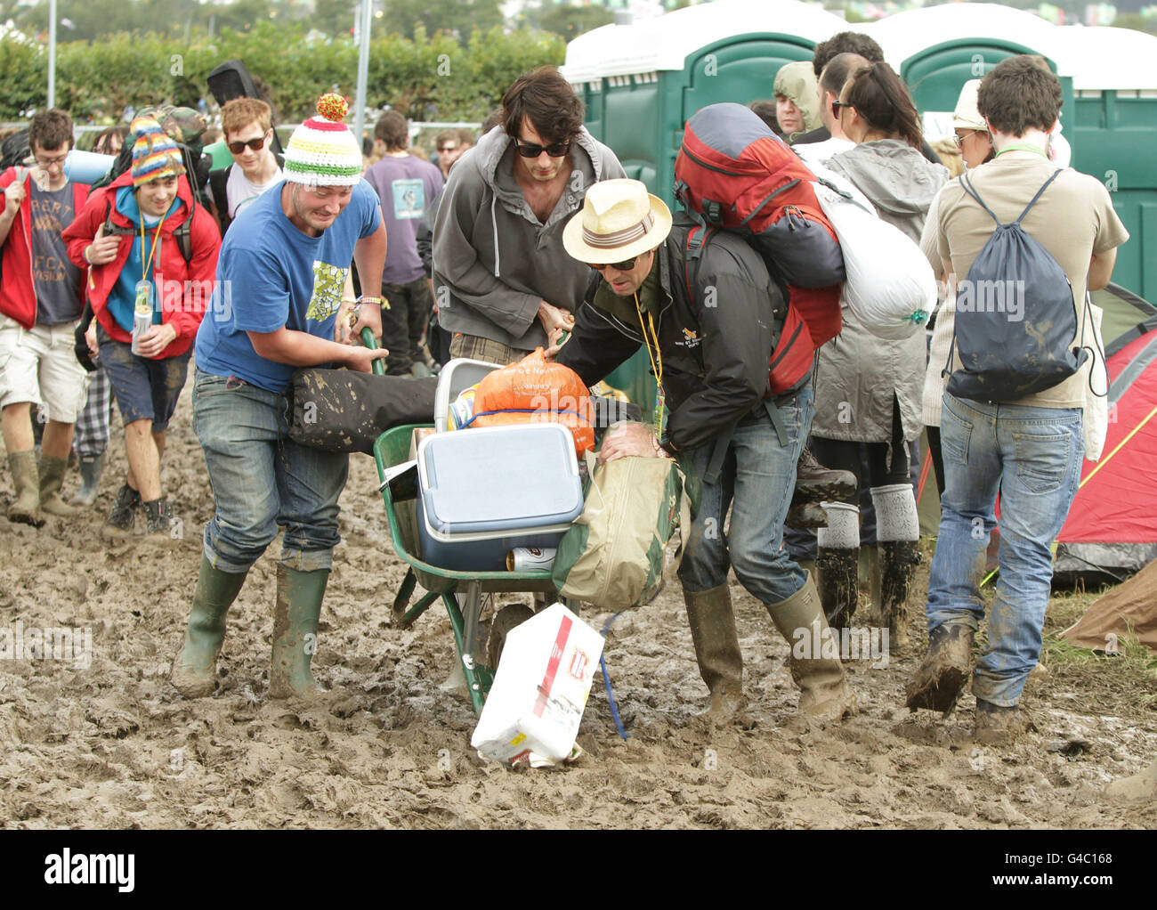 Revellers drop a crate of beer while using a wheelbarrow in the mud at ...
