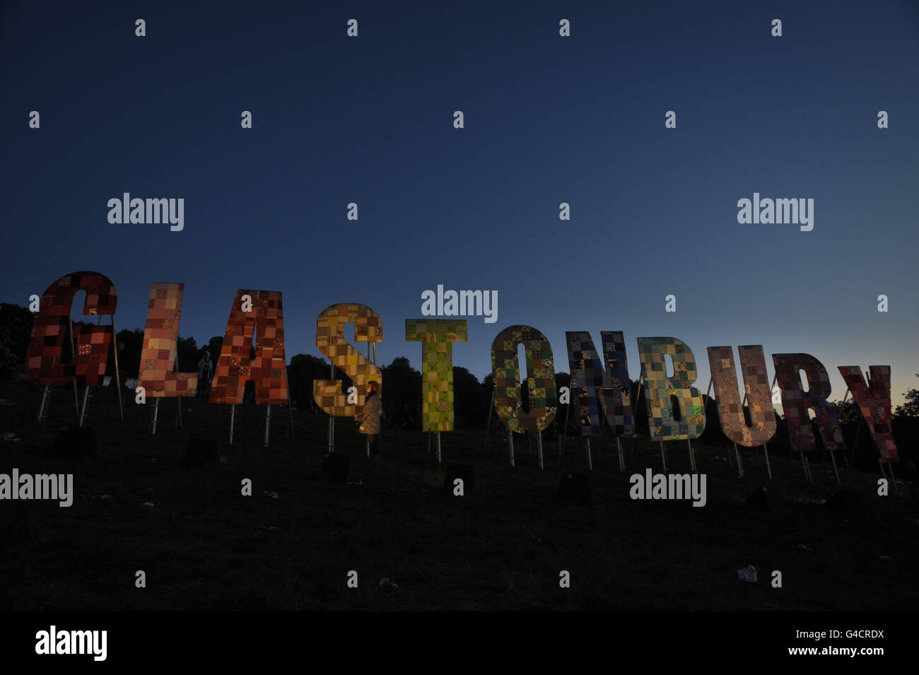A woman stands by the Glastonbury sign during sunset near the Park area ...