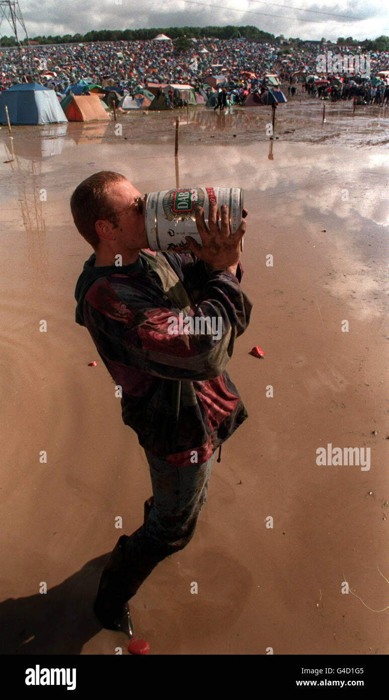 A FESTIVAL GOER ENJOYS A BIG DRINK OF A BEER AT A MUD AND RAIN SOAKED ...