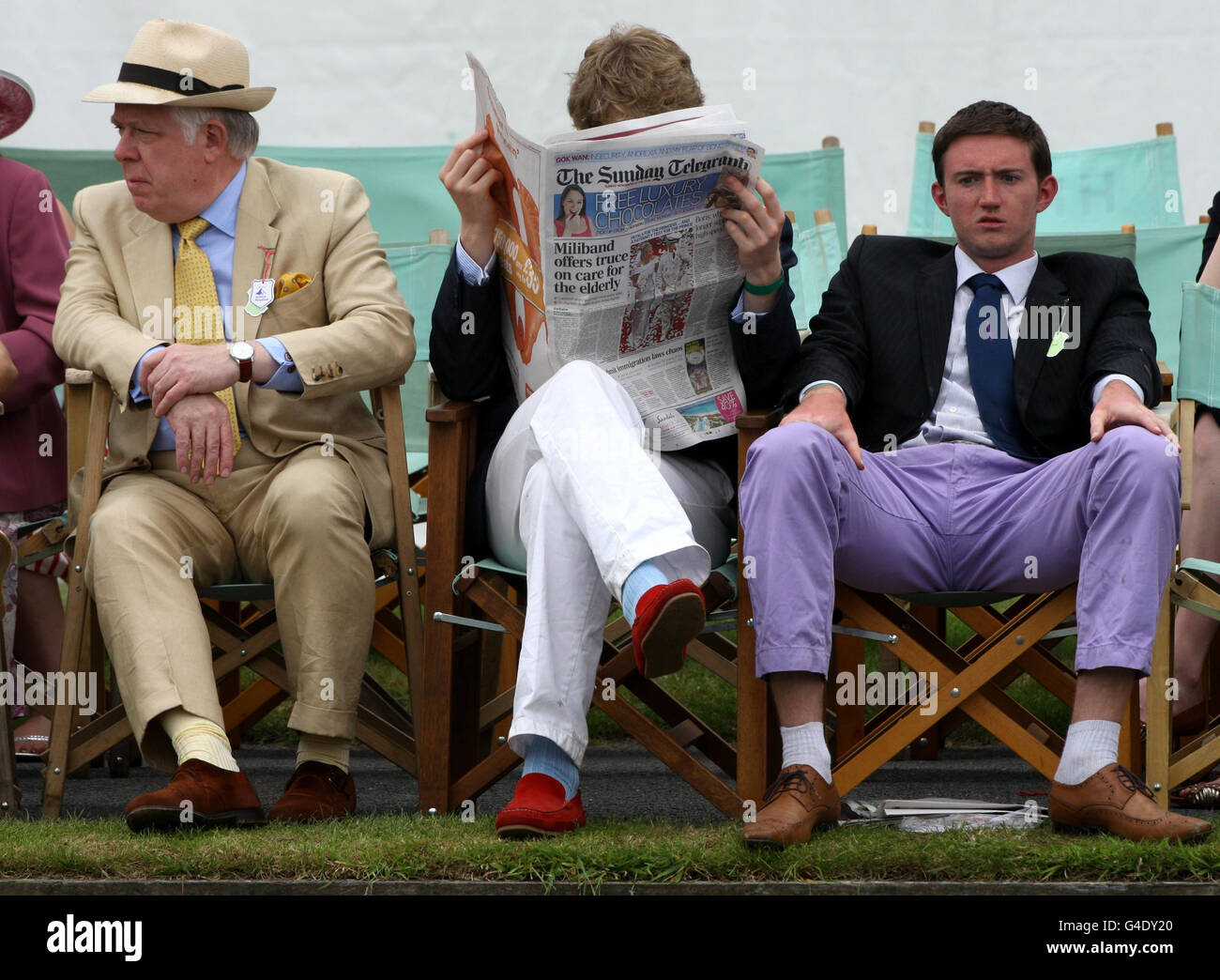 Male spectators at Henley Royal Regatta watch the rowing and read a ...