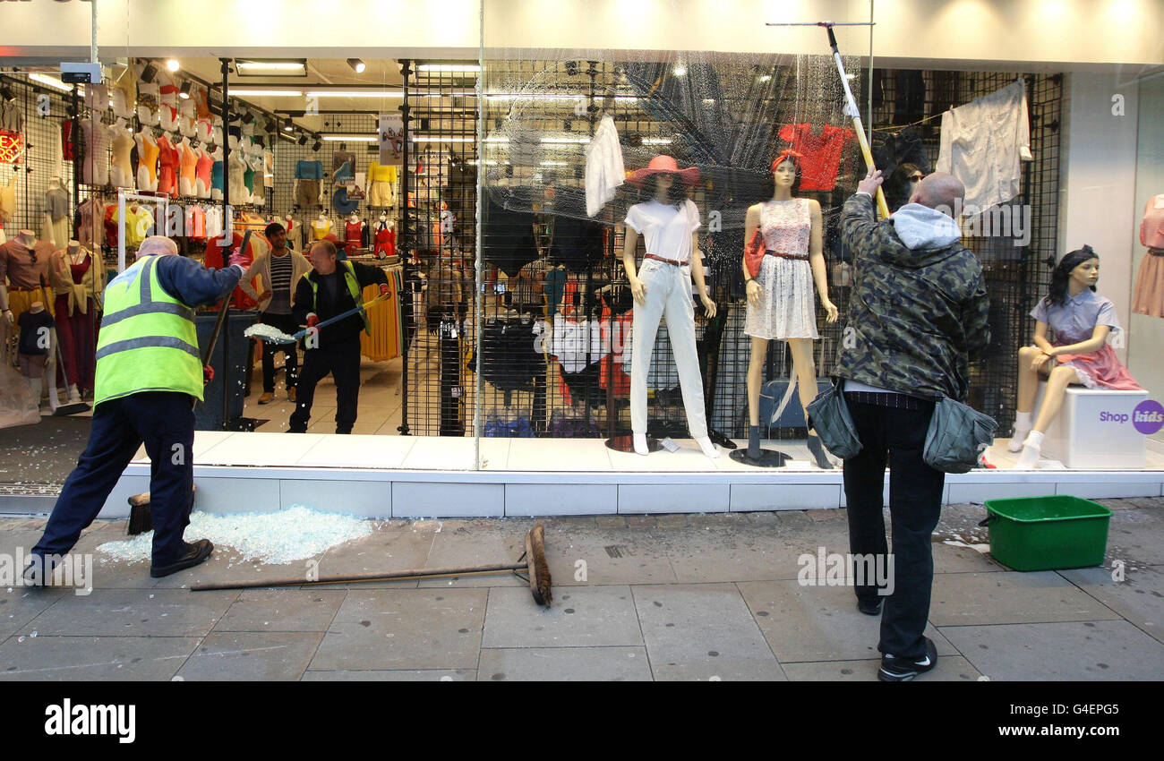 A council workers clears up broken glass as a window cleaner cleans the ...