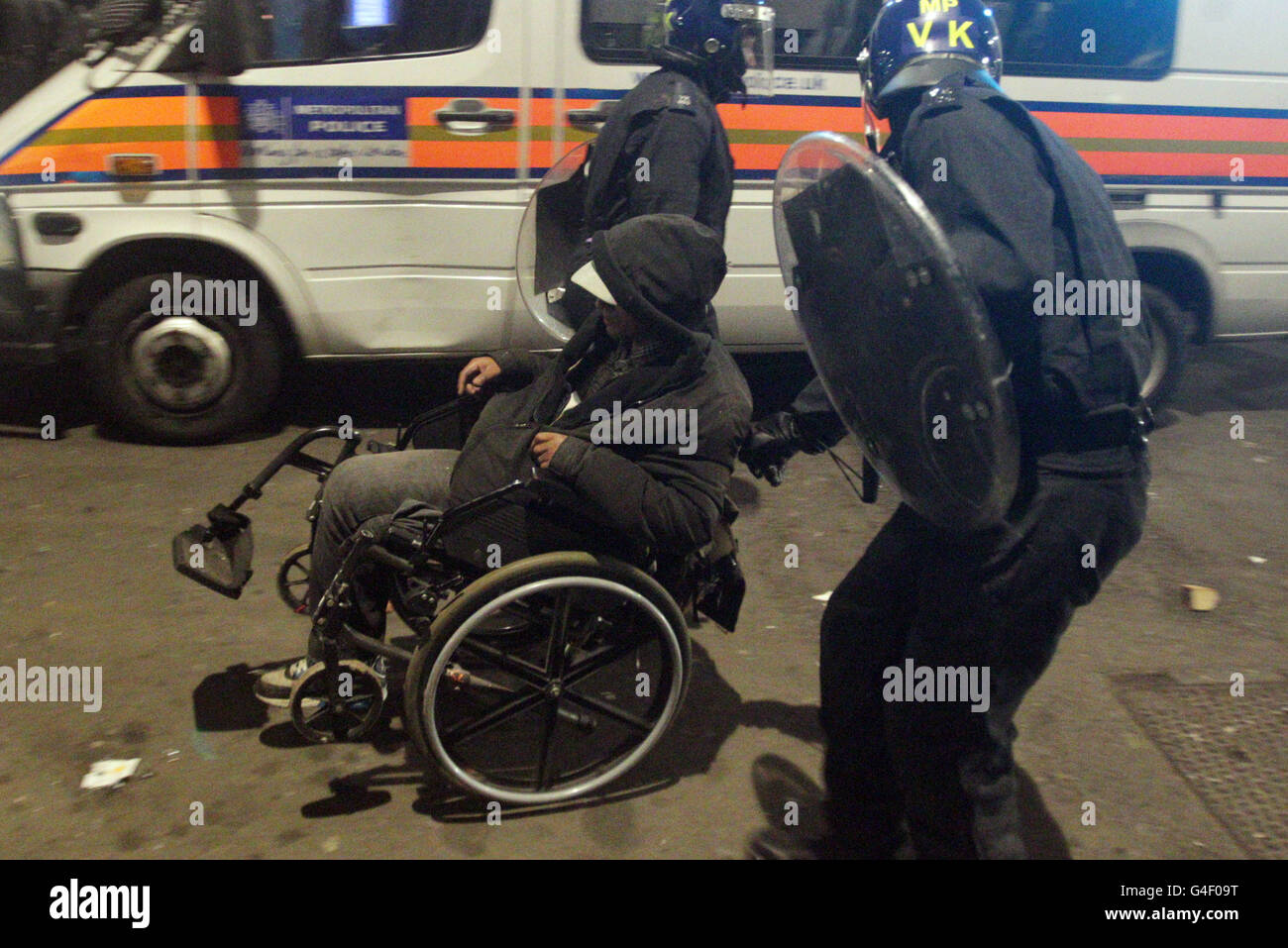 A man in a wheelchair is helped by riot police in Tottenham, north ...