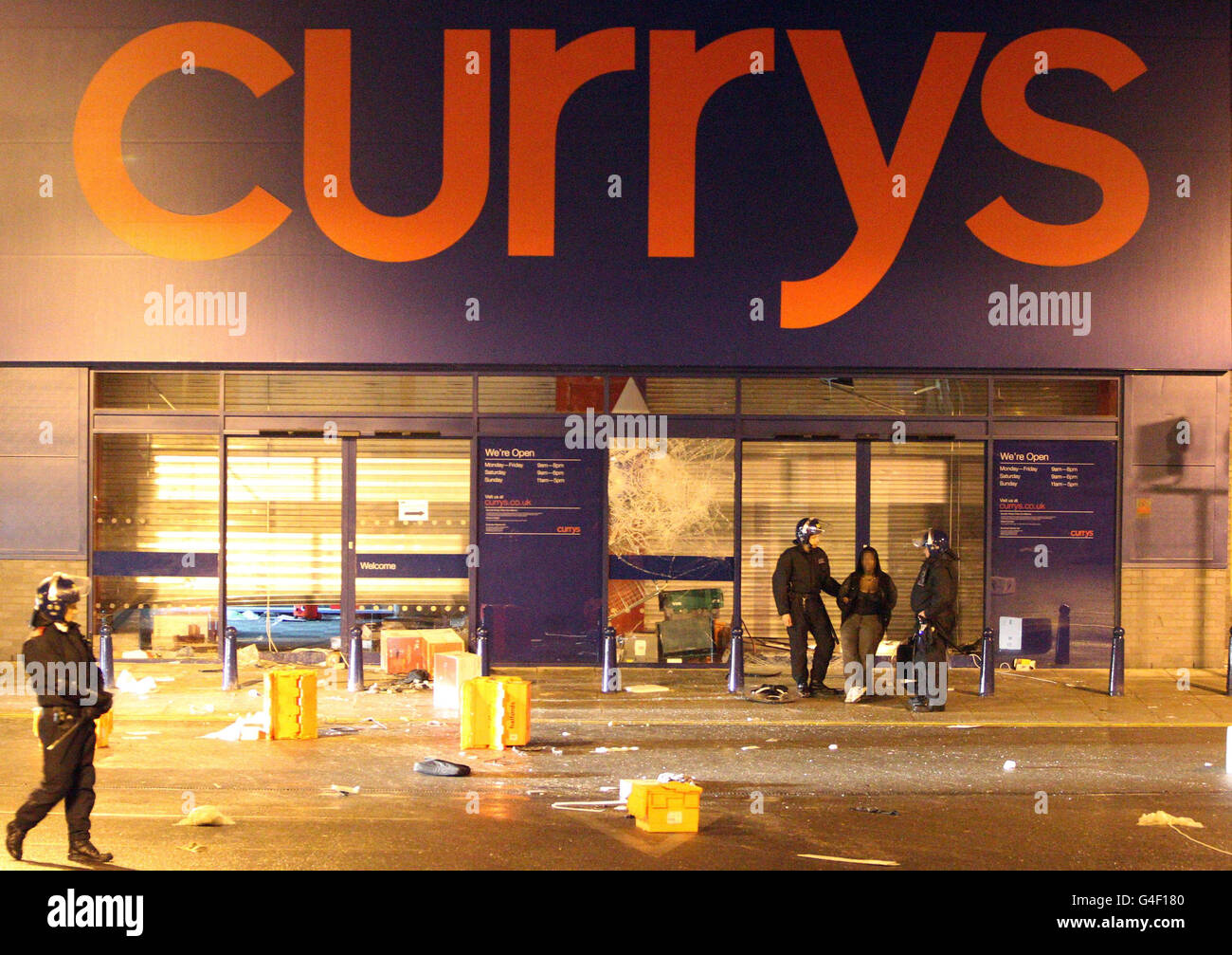 Police detain a woman outside a Currys store whose windows had been ...