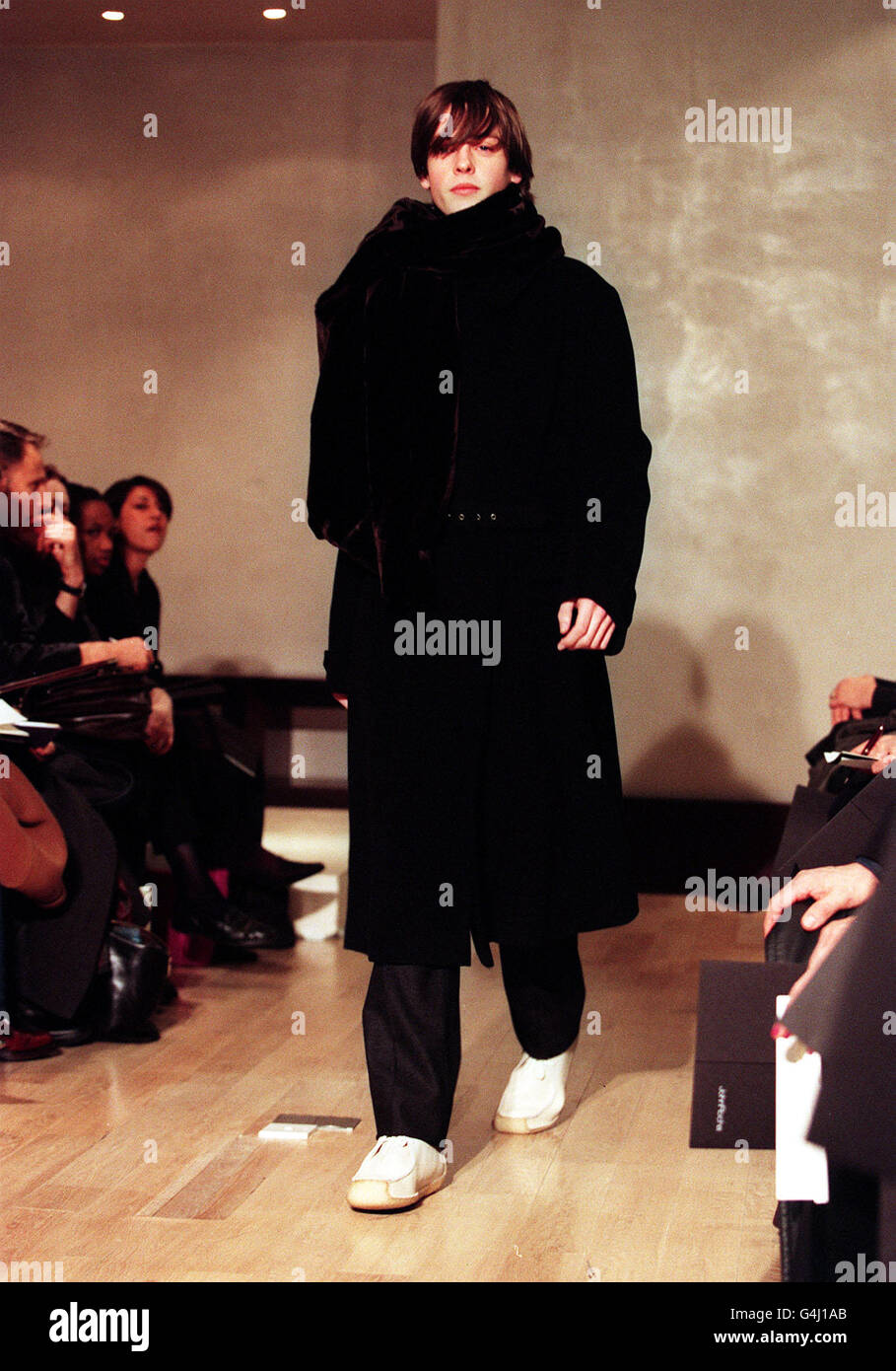 A model presents a dark grey coat and trousers with velvet scarf ...