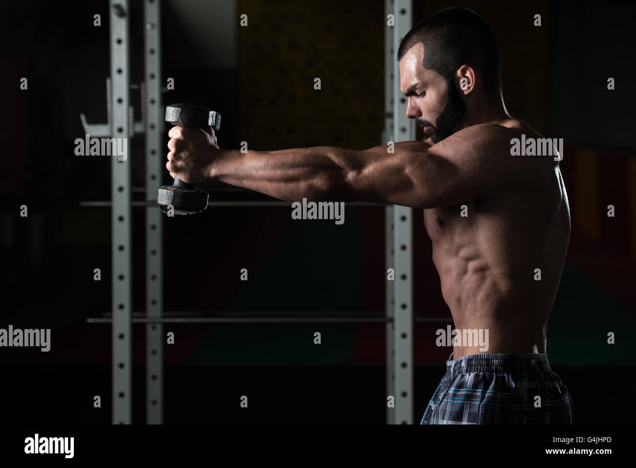 Young Man Working Out Shoulders In A Dark Gym - Bodybuilder Doing Heavy ...