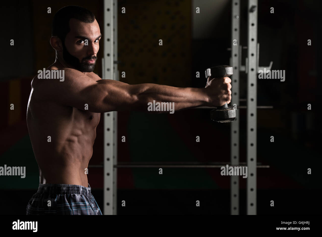 Young Man Working Out Shoulders In A Dark Gym - Bodybuilder Doing Heavy ...