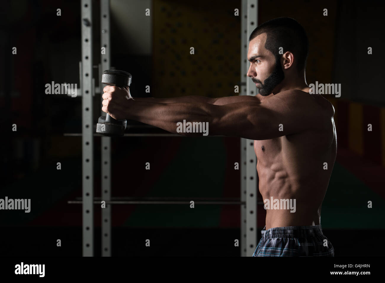 Young Man Working Out Shoulders In A Dark Gym - Bodybuilder Doing Heavy ...