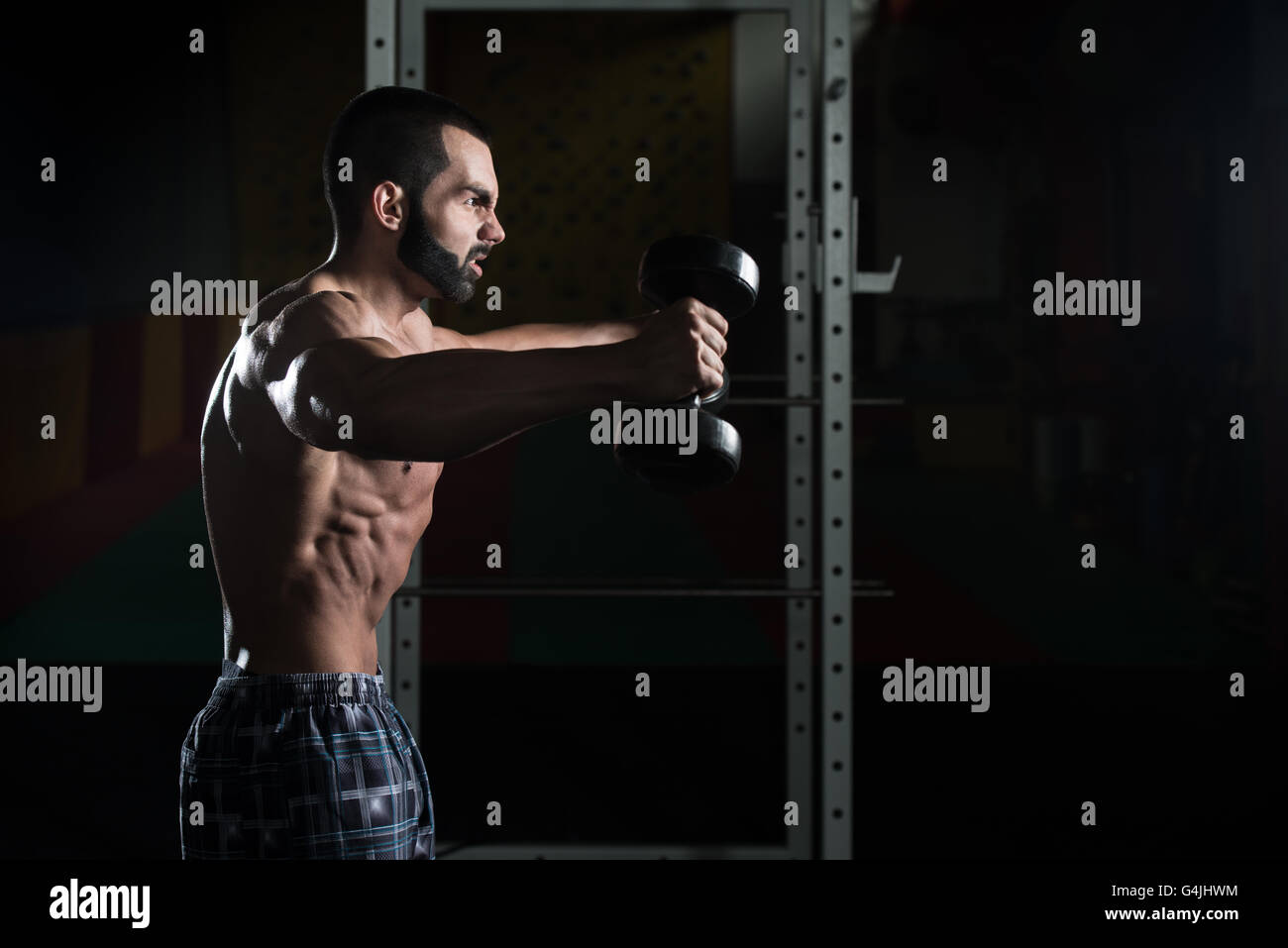 Young Man Working Out Shoulders In A Dark Gym - Bodybuilder Doing Heavy ...