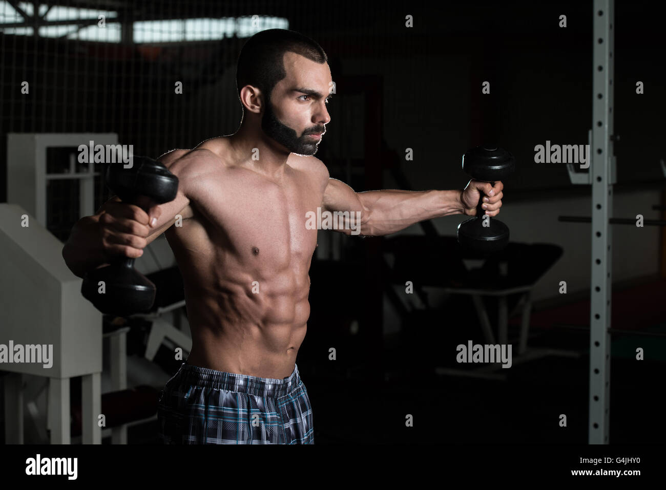 Young Man Working Out Shoulders In A Dark Gym - Bodybuilder Doing Heavy ...
