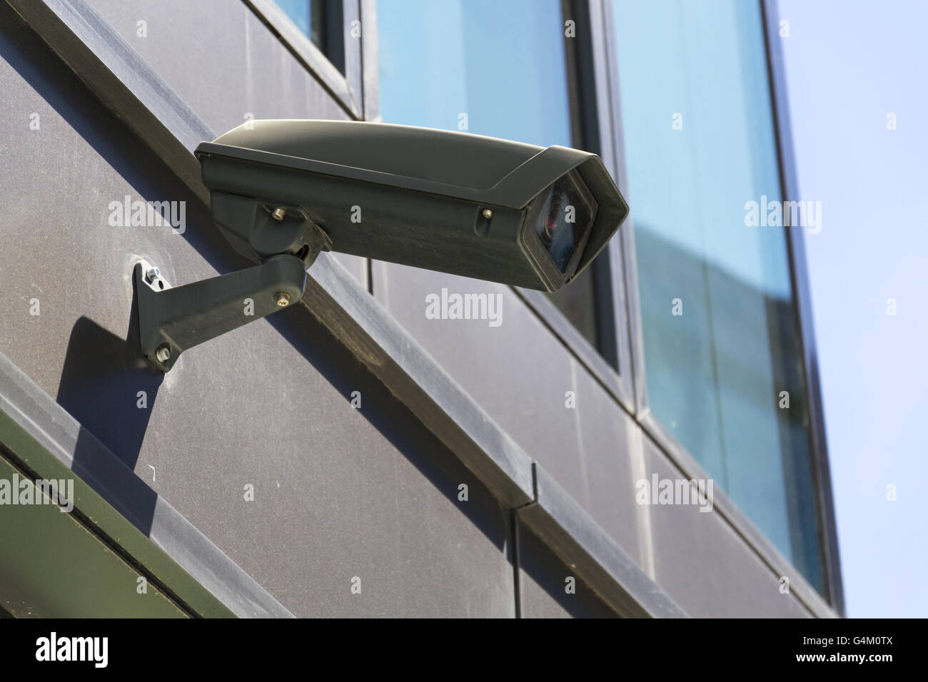 Grey security camera attached to wall blue windows background Stock ...