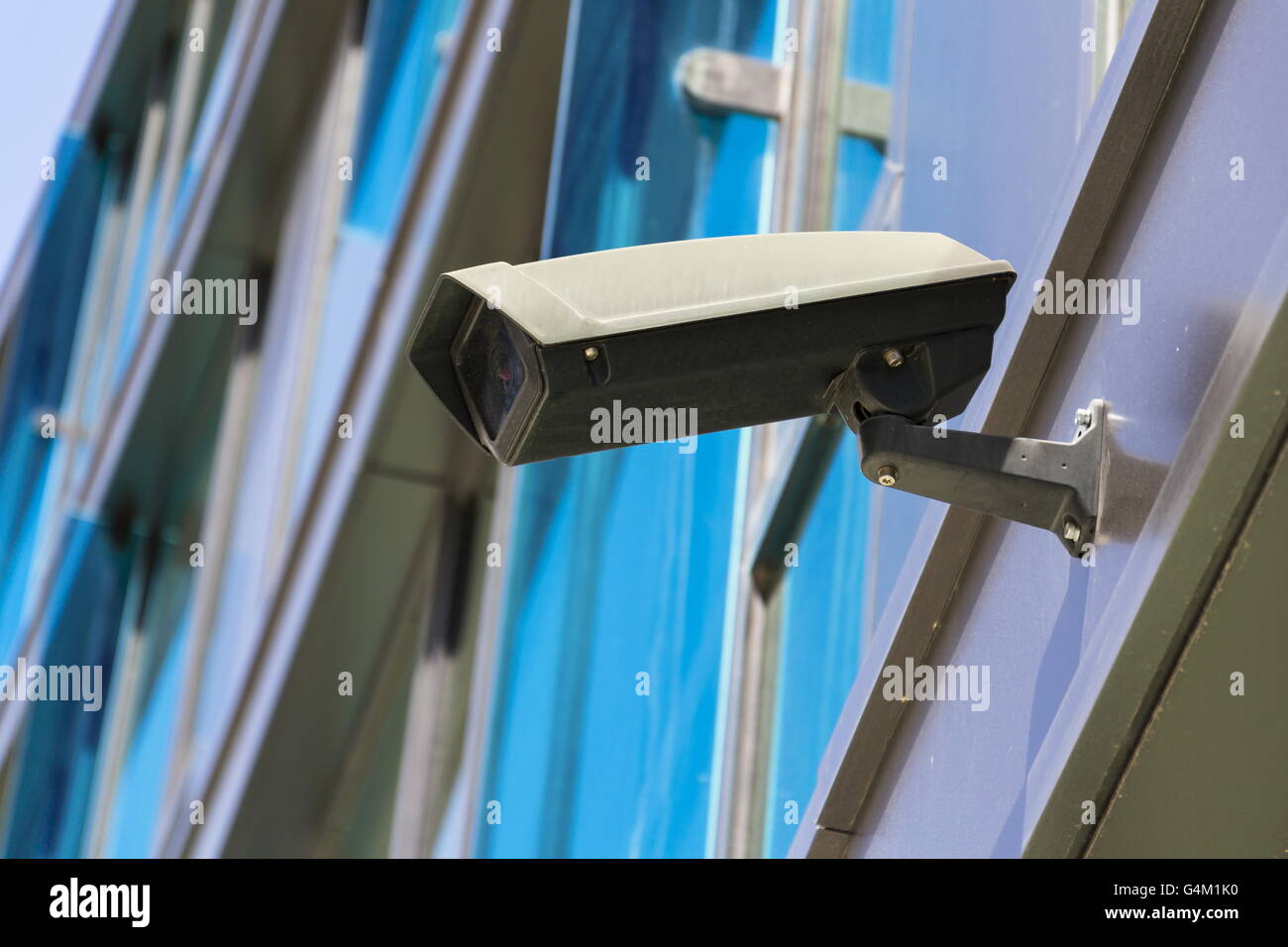 Grey security camera attached to wall blue windows background Stock ...