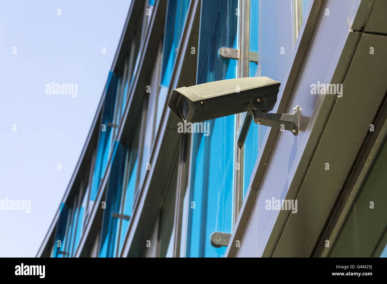 Grey security camera attached to wall blue windows background Stock ...
