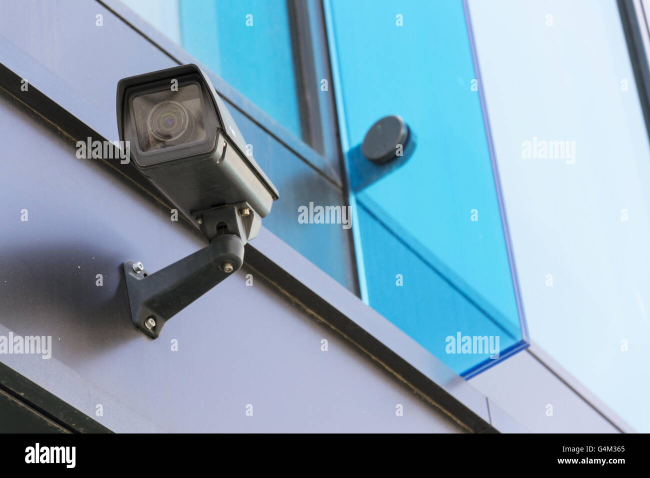 Grey security camera attached to wall blue windows background Stock ...