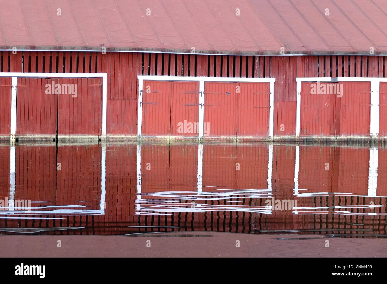 Red wooden boat storage building by a lake. Reflections of the doors ...