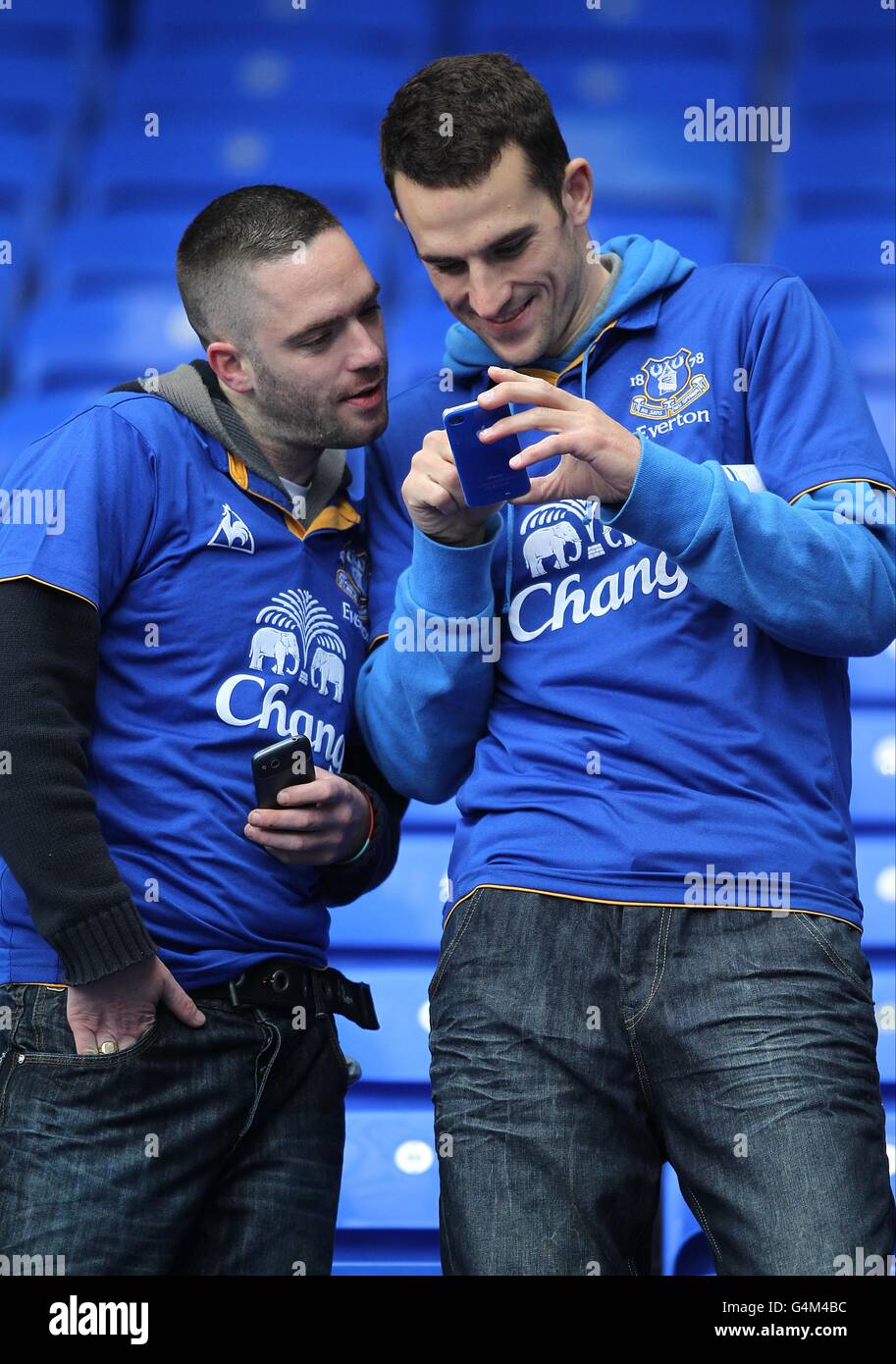 Two Everton fans look at their mobile phones in the stands Stock Photo ...