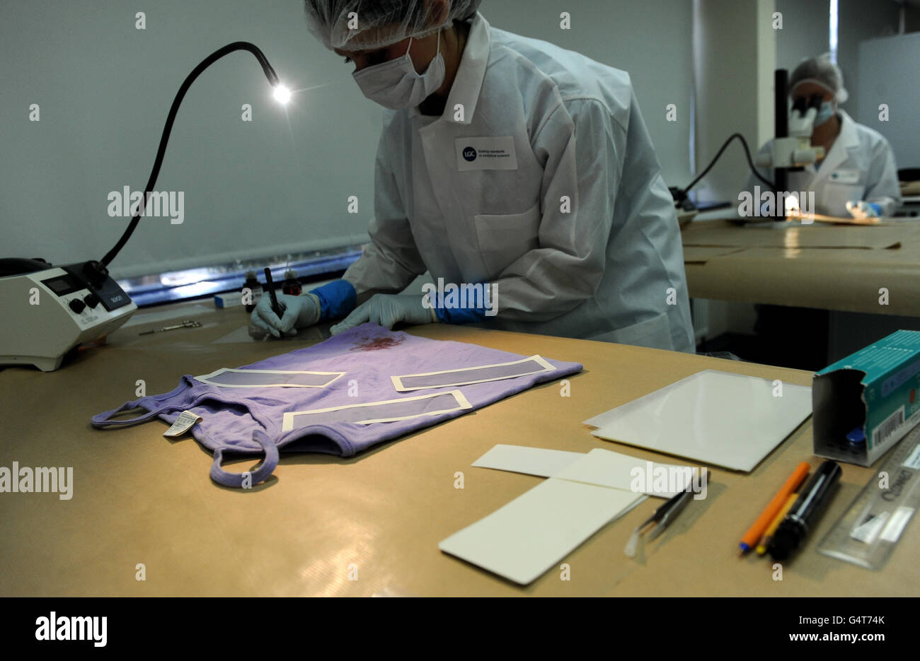 A forensic scientist collects blood and fibers from an item of clothing ...