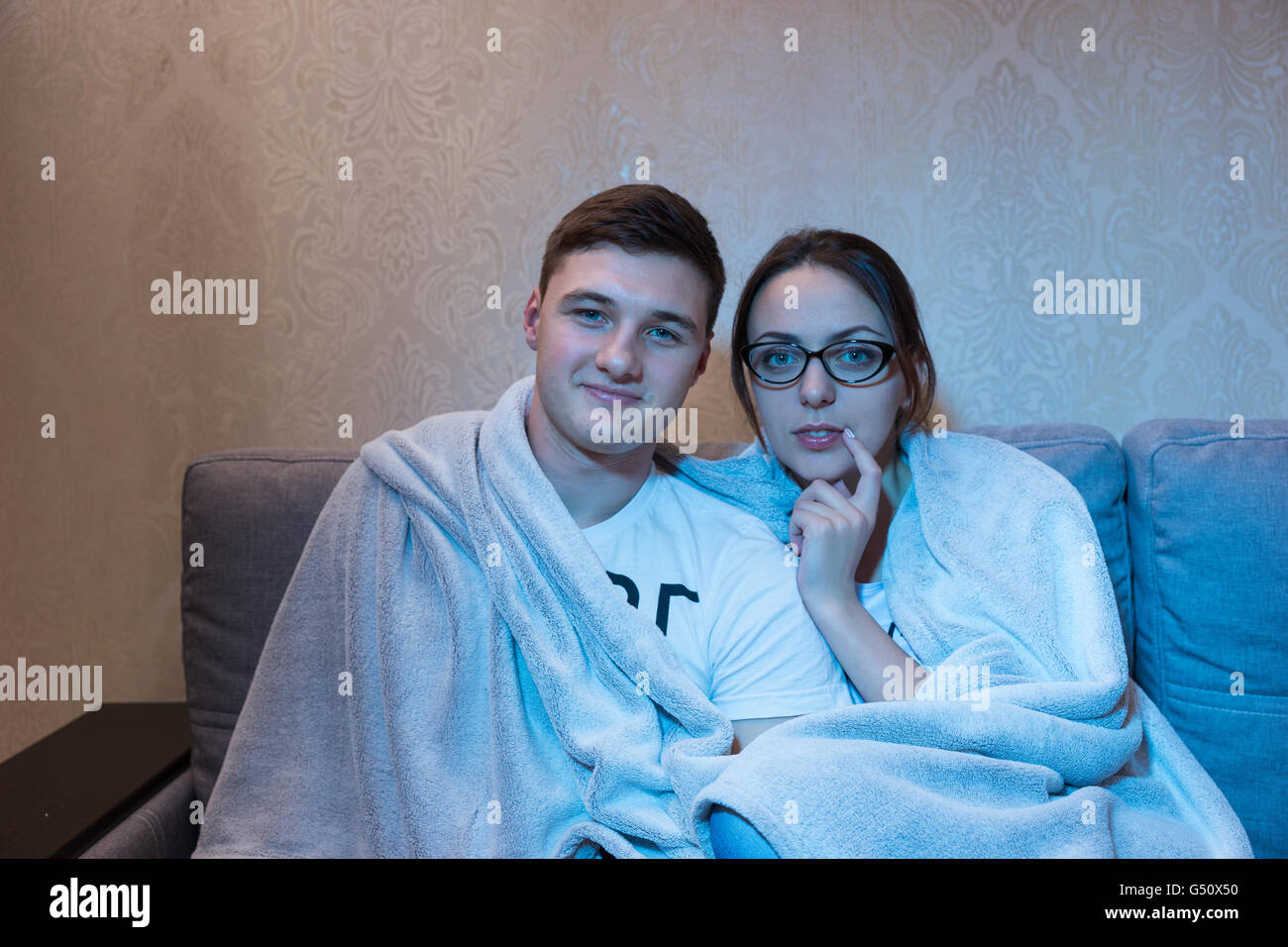 Young attrsctive couple snuggling up together under a blanket on a sofa ...