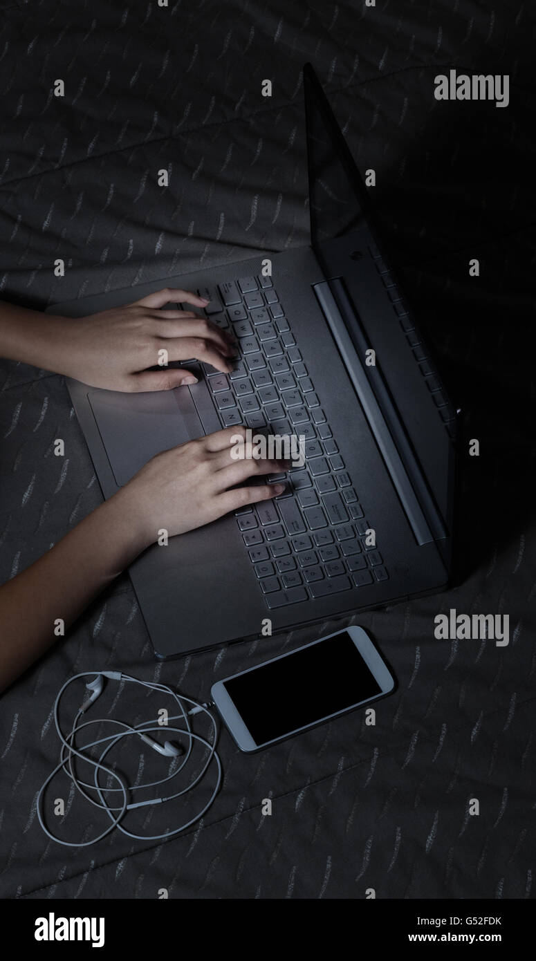 Hands typing on computer while at nighttime in bed. Light effect on ...