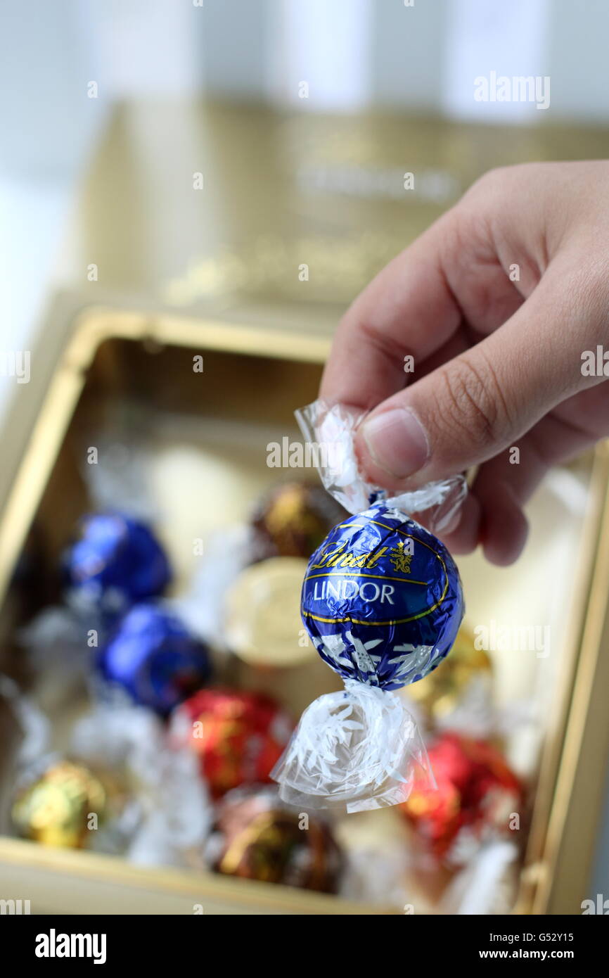 Close up of hand holding blue wrapped Lindt Lindor Chocolate with gold ...