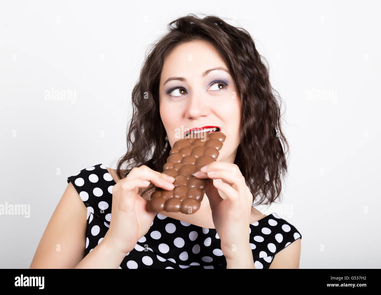 Beautiful young woman eating a chocolate bar, wears a dress with polka ...