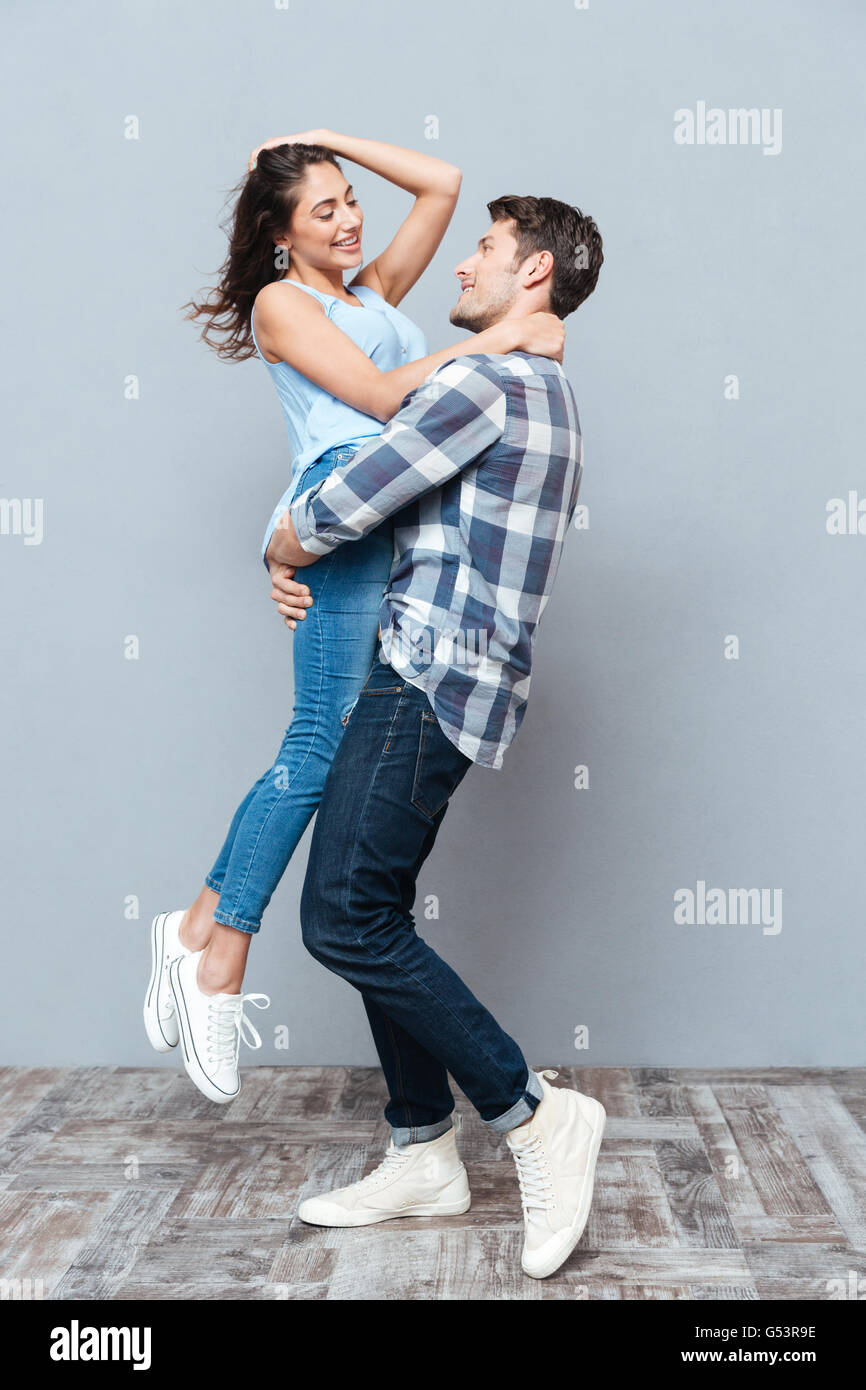Handsome man picking up and hugging his girlfriend isolated on gray ...