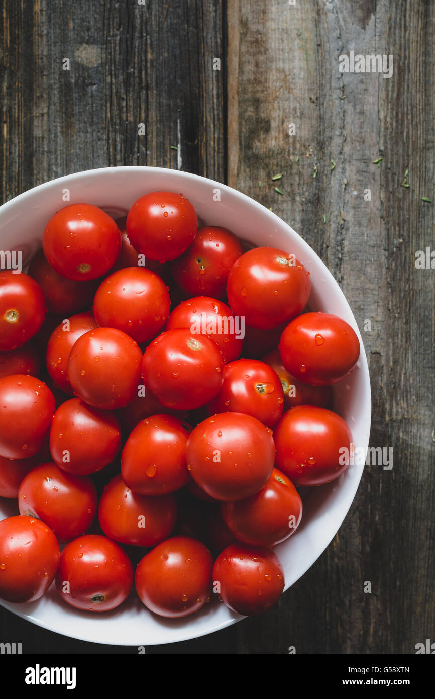 Cherry tomatoes covered with water drops in white bowl on rustic wooden backdrop. Top view ...
