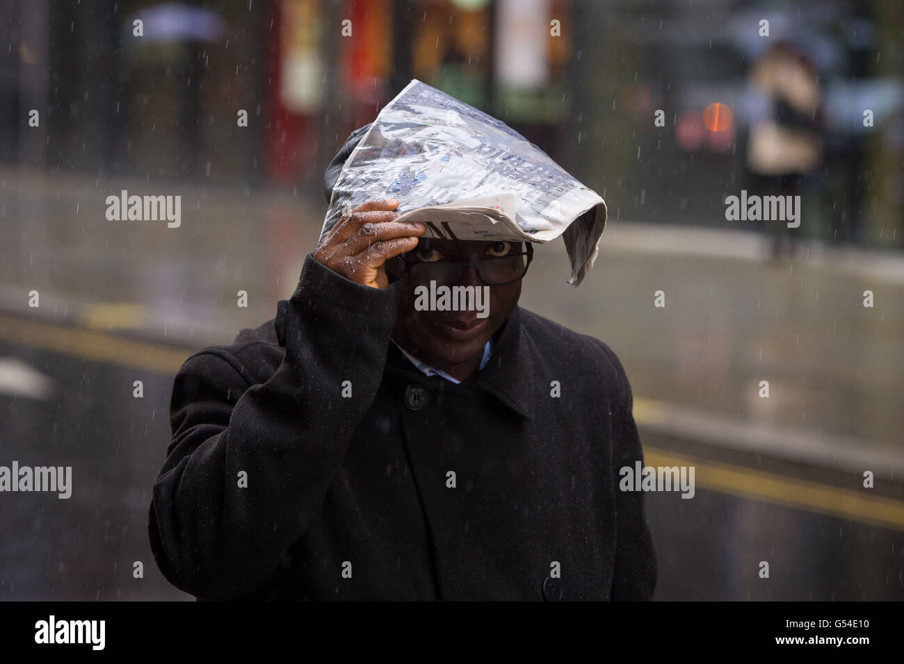 A man shelters under a newspaper in central London, as heavy rain and ...