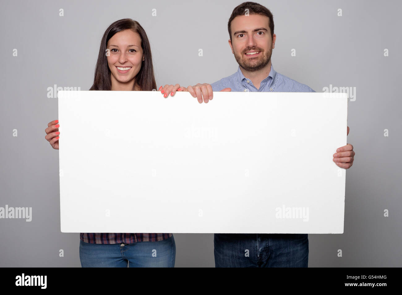 Young Lovers Couple Holding A White Cardboard Isolated On Gray