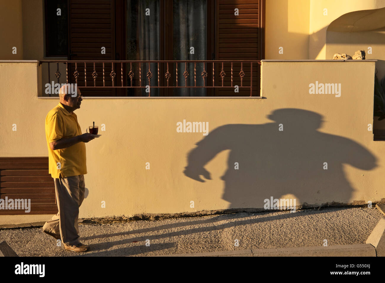 A middle aged man casts a shadow as he walks with a cup of tea through ...