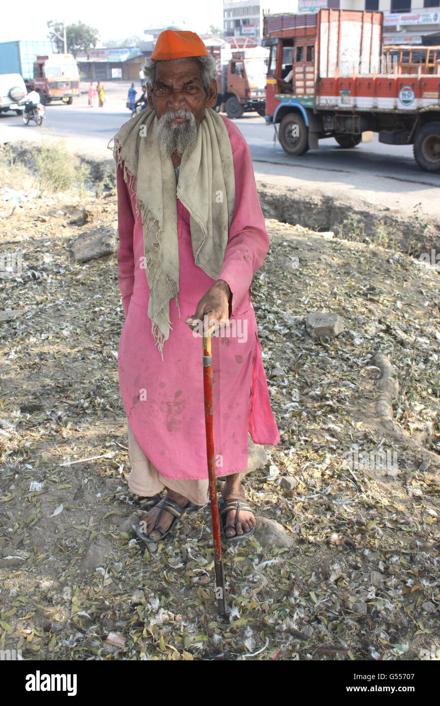 An old poor man from India on the streetside walking with his stick ...