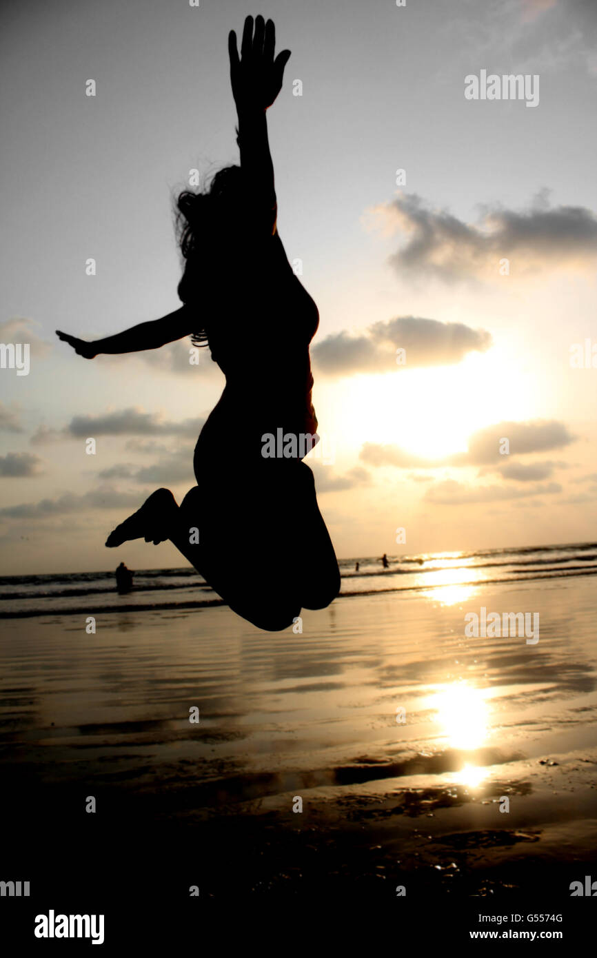 A silhouette of a woman jumping freely with her hands stretched, at ...