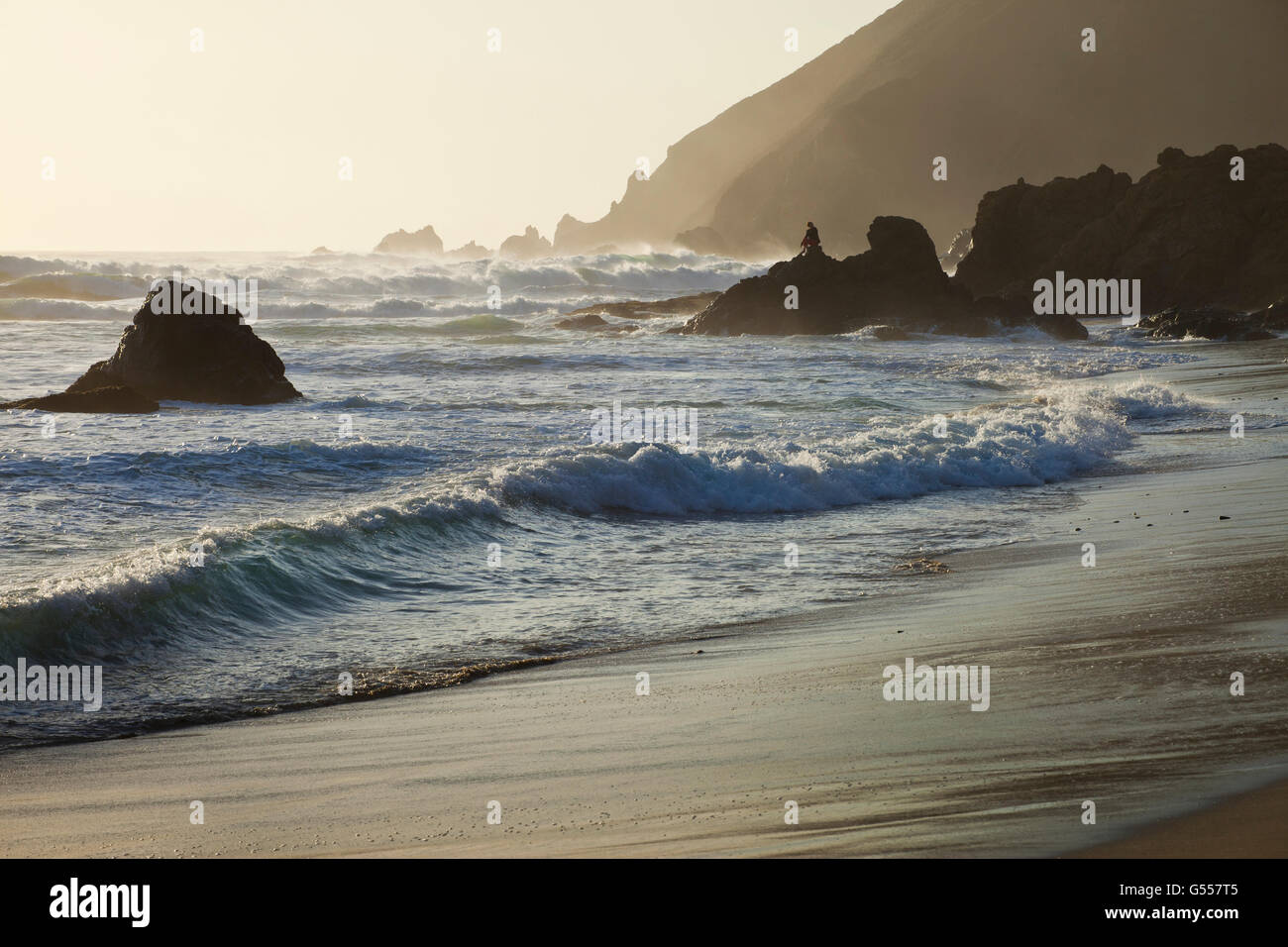 Young woman sitting on rock overlooking surf near sunset, Pfeiffer ...