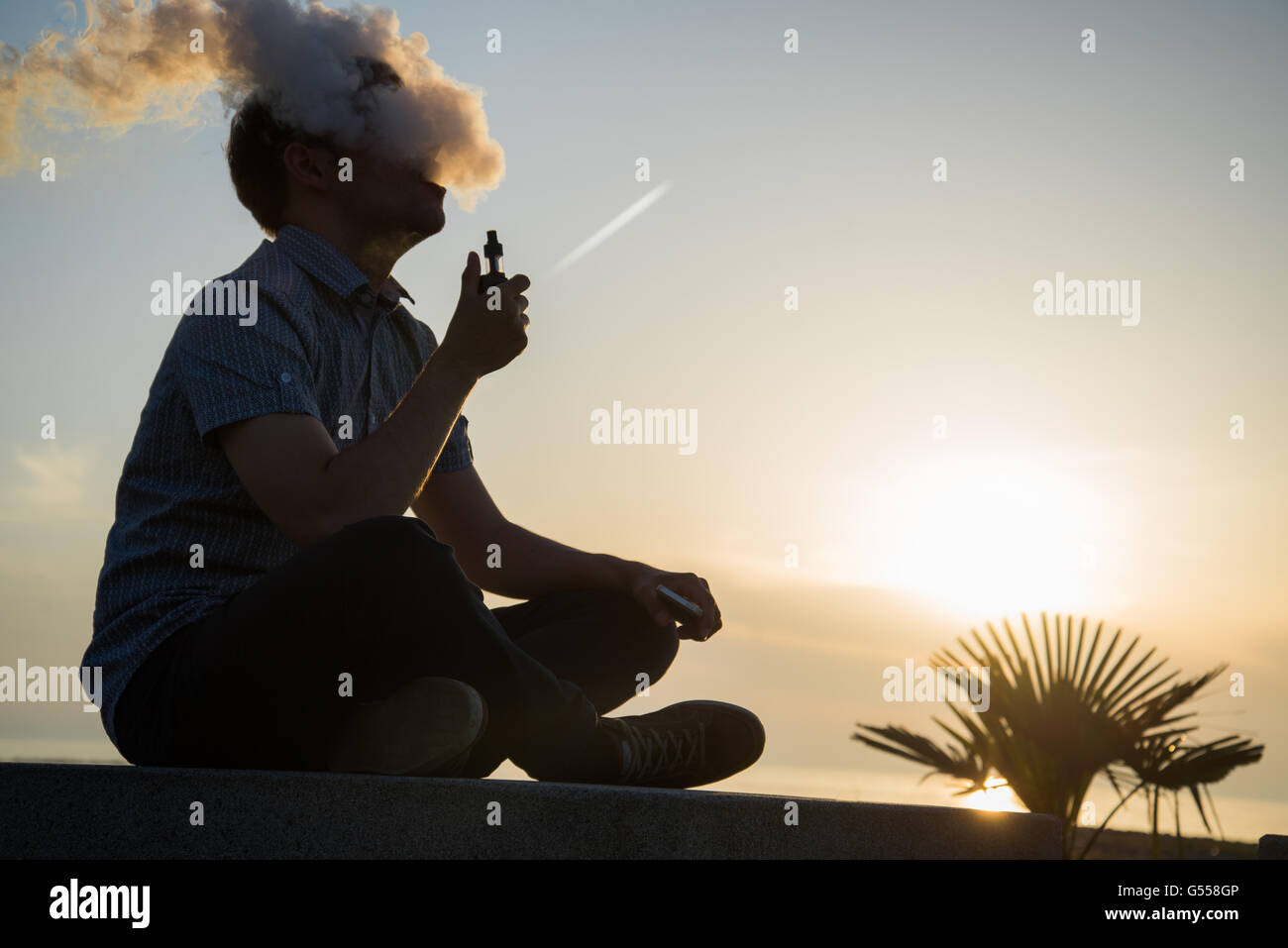 vaping young man with, produces vapor on sunset sky background at the ...