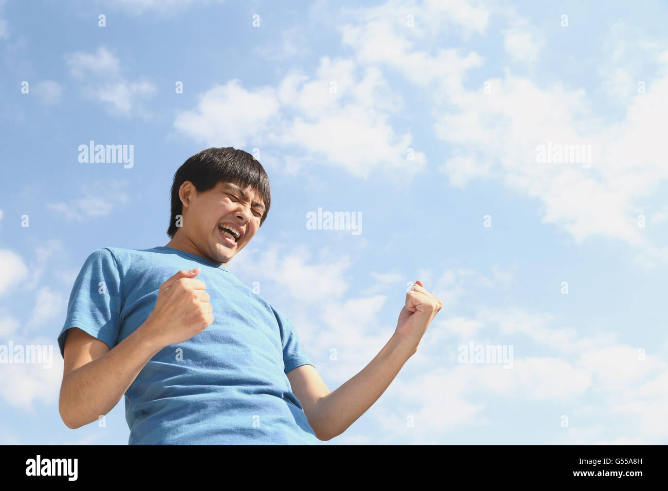 Young Japanese man cheering against blue sky Stock Photo - Alamy
