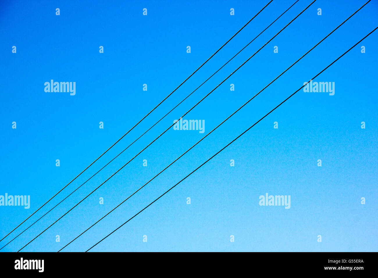 Five electric electricity supply cables stretching across blue sky ...