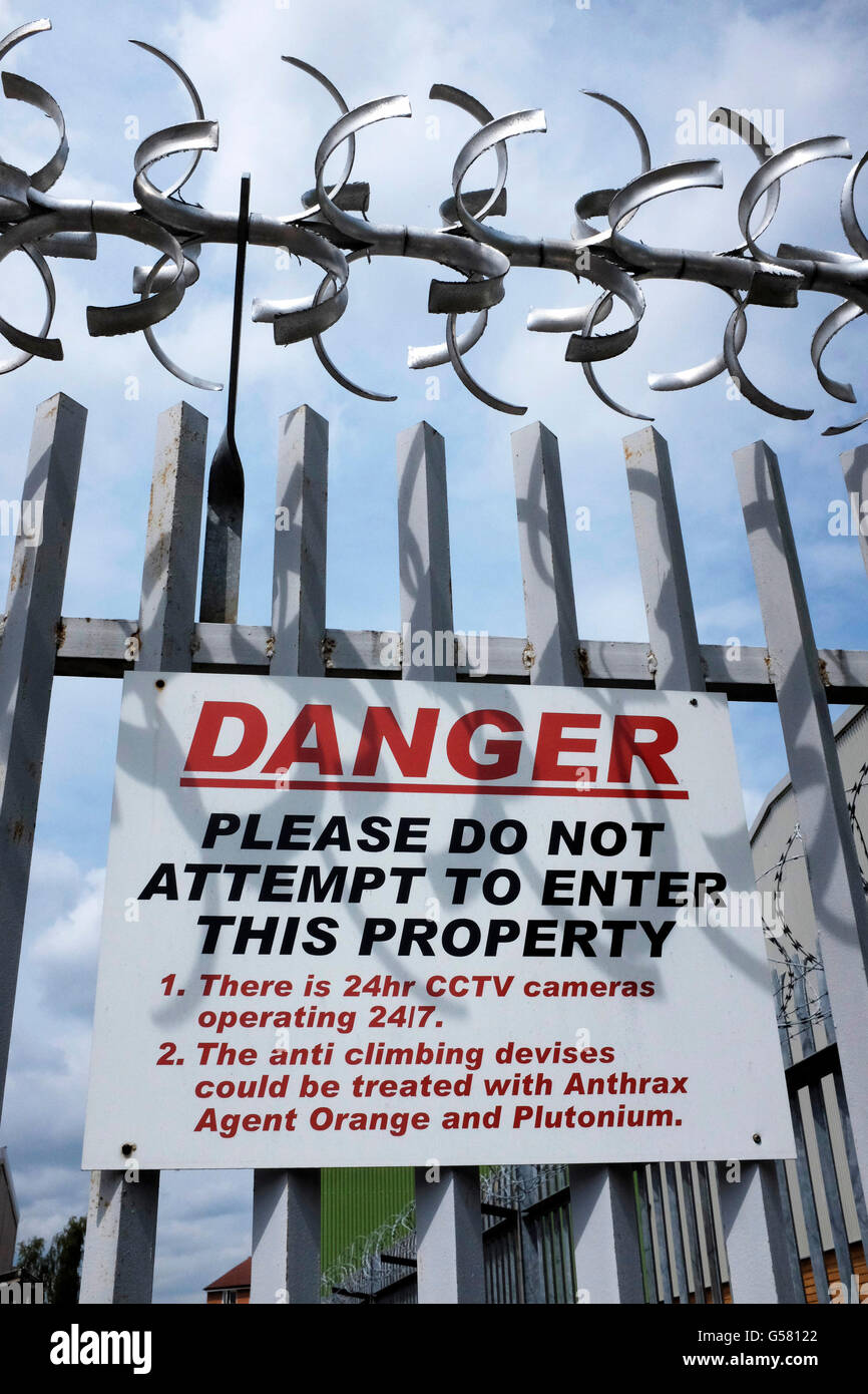 Alarming danger notice on a security fence outside an industrial estate ...
