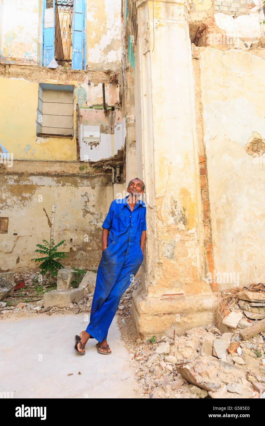 Cuban man in blue worker's boilersuit leaning against wall in the ruins ...