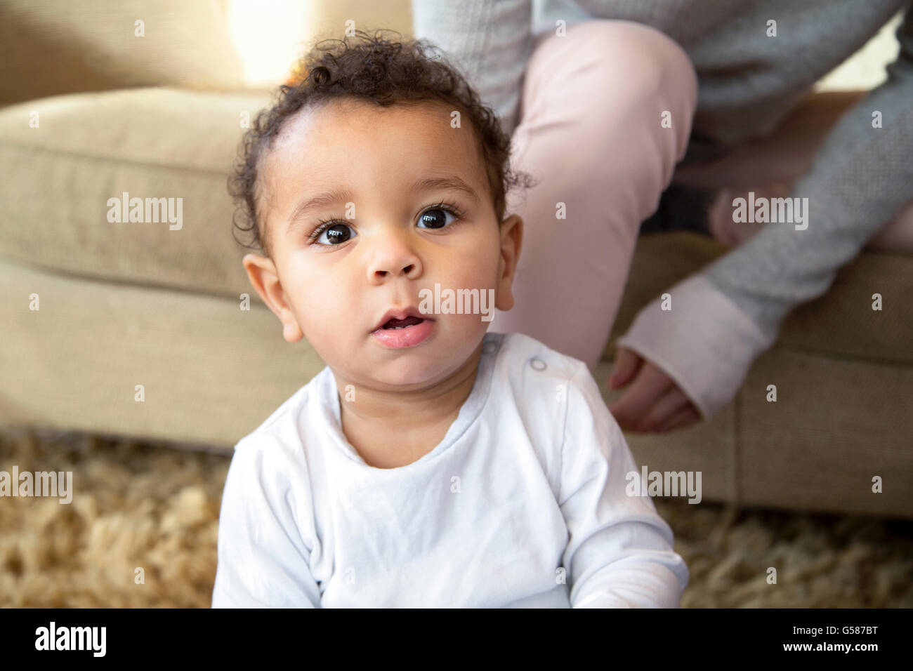 Baby boy sitting on the floor of his front room with his mother sitting ...