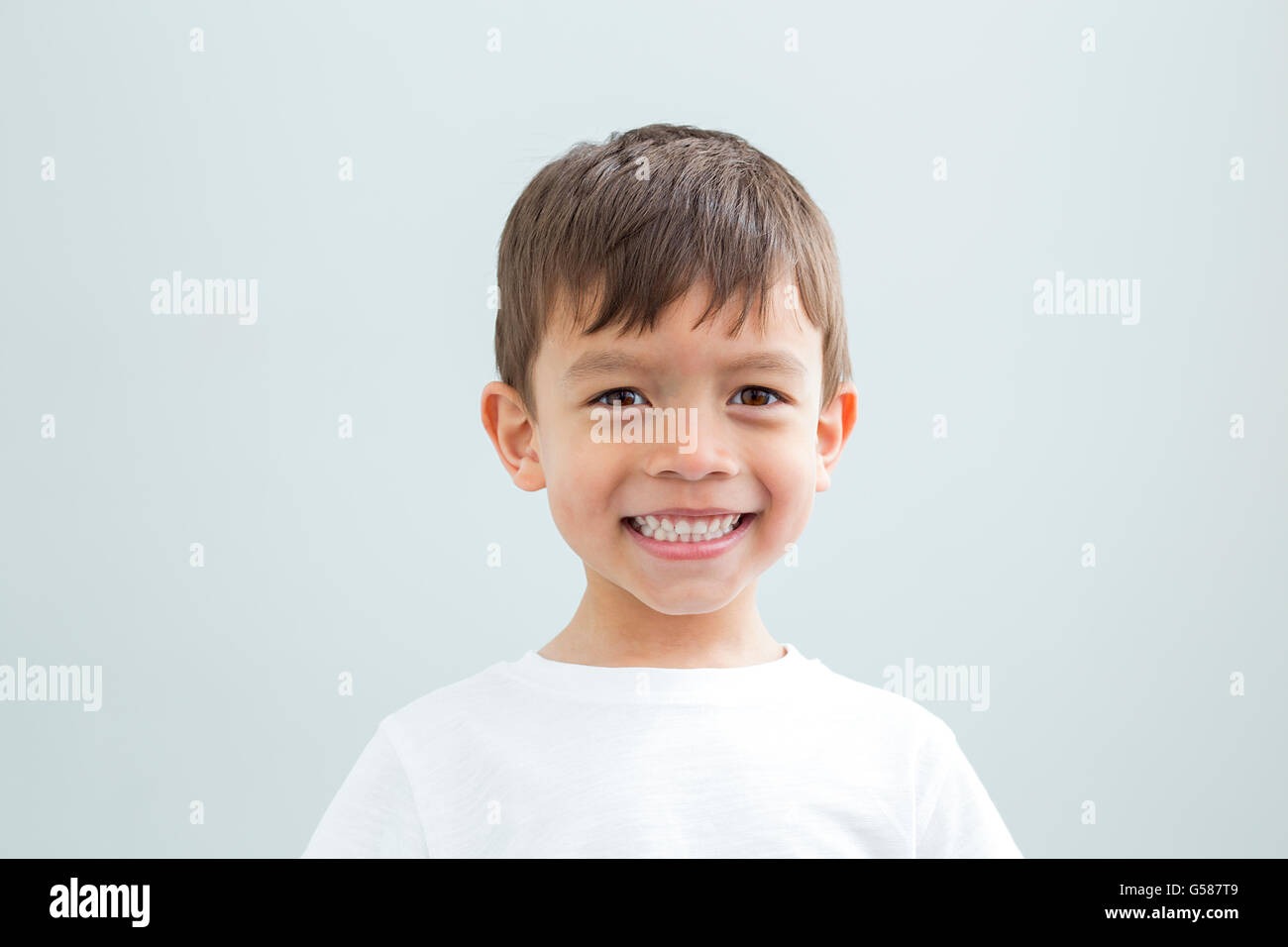 Landscape head shot of a young boy on a plain background. He is smiling ...