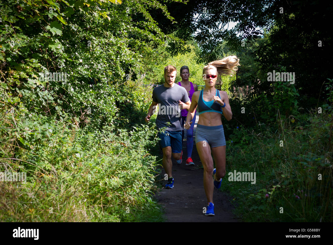 Three people of different ages running outdoors along a woodland path ...