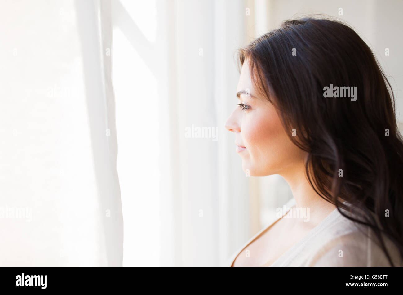 young woman looking through window at home Stock Photo - Alamy