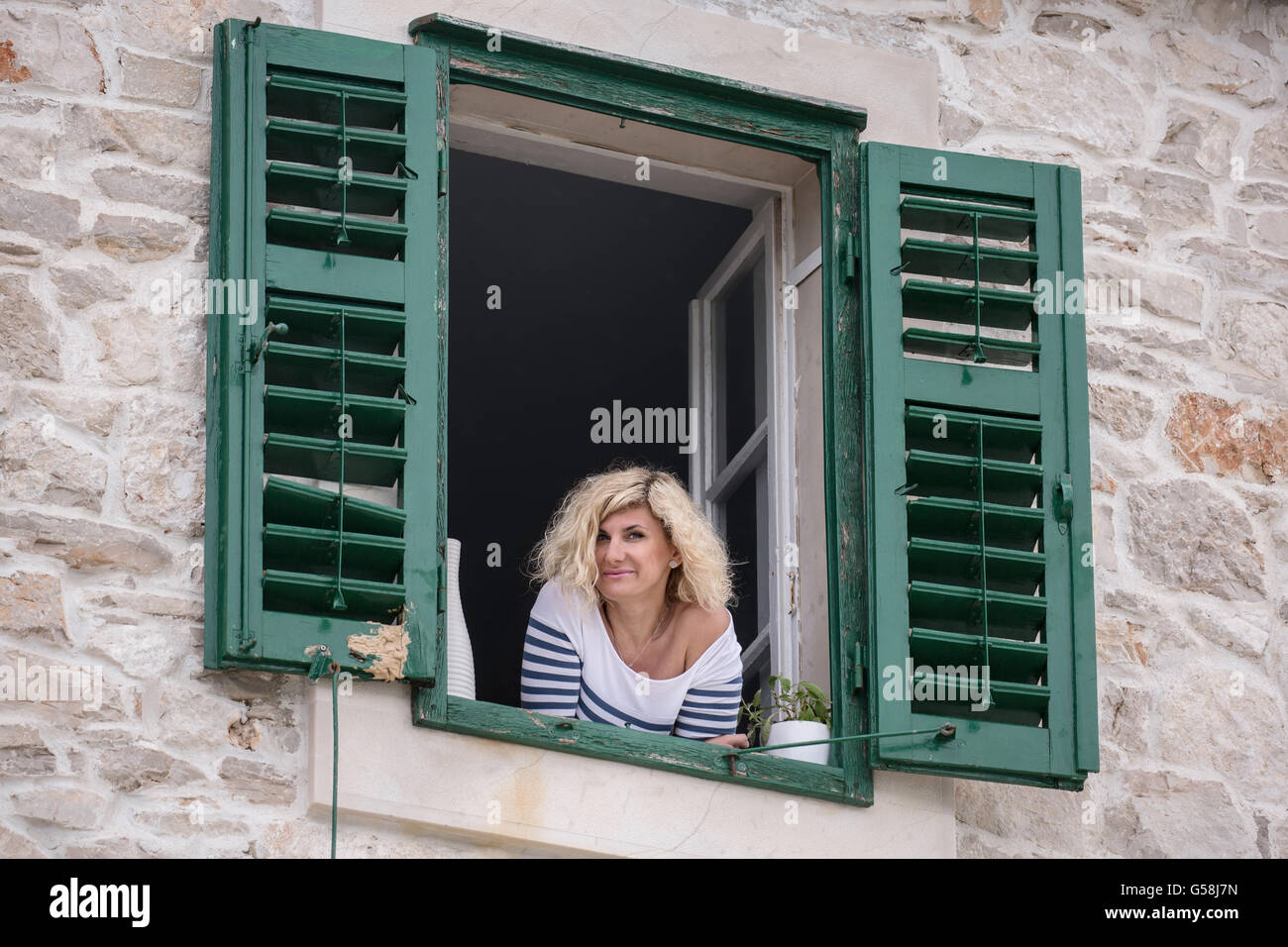Beautiful blonde woman is looking out the window, leaning on the ...
