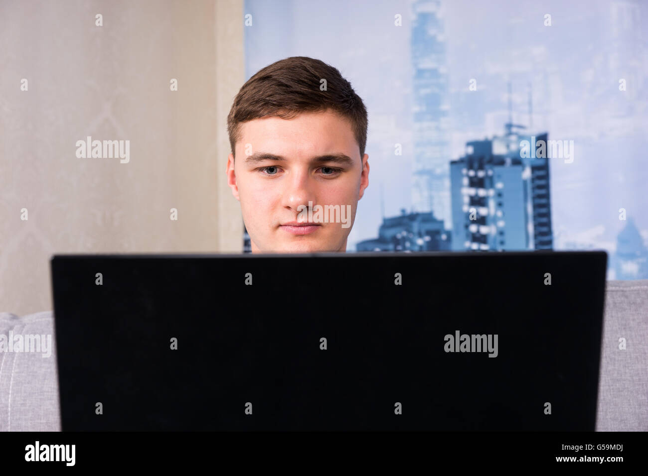 Handsome man working and sitting behind a laptop on a couch doing his ...