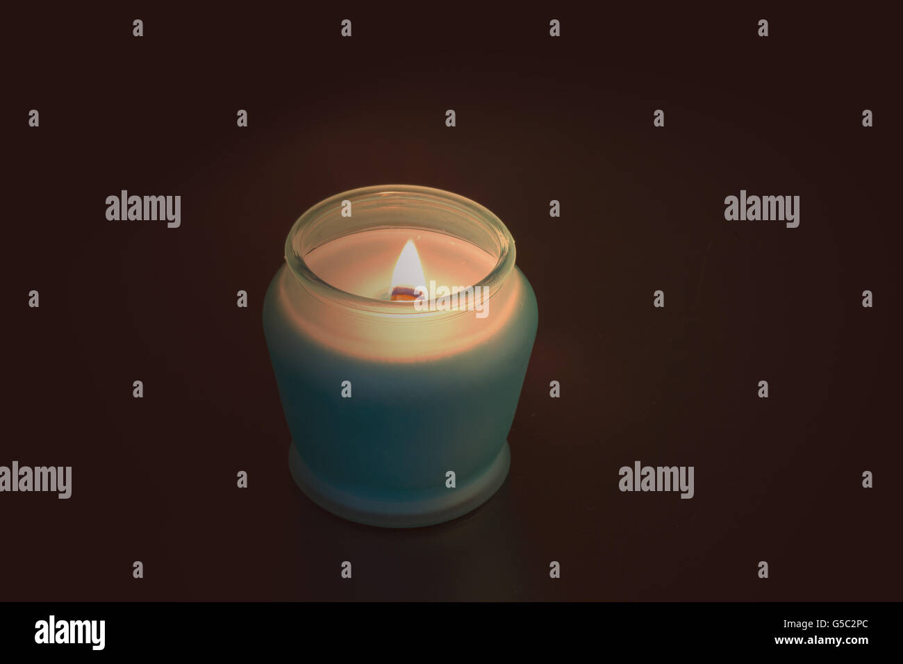 A candle glows in the dark, providing a room with low, romantic light ...