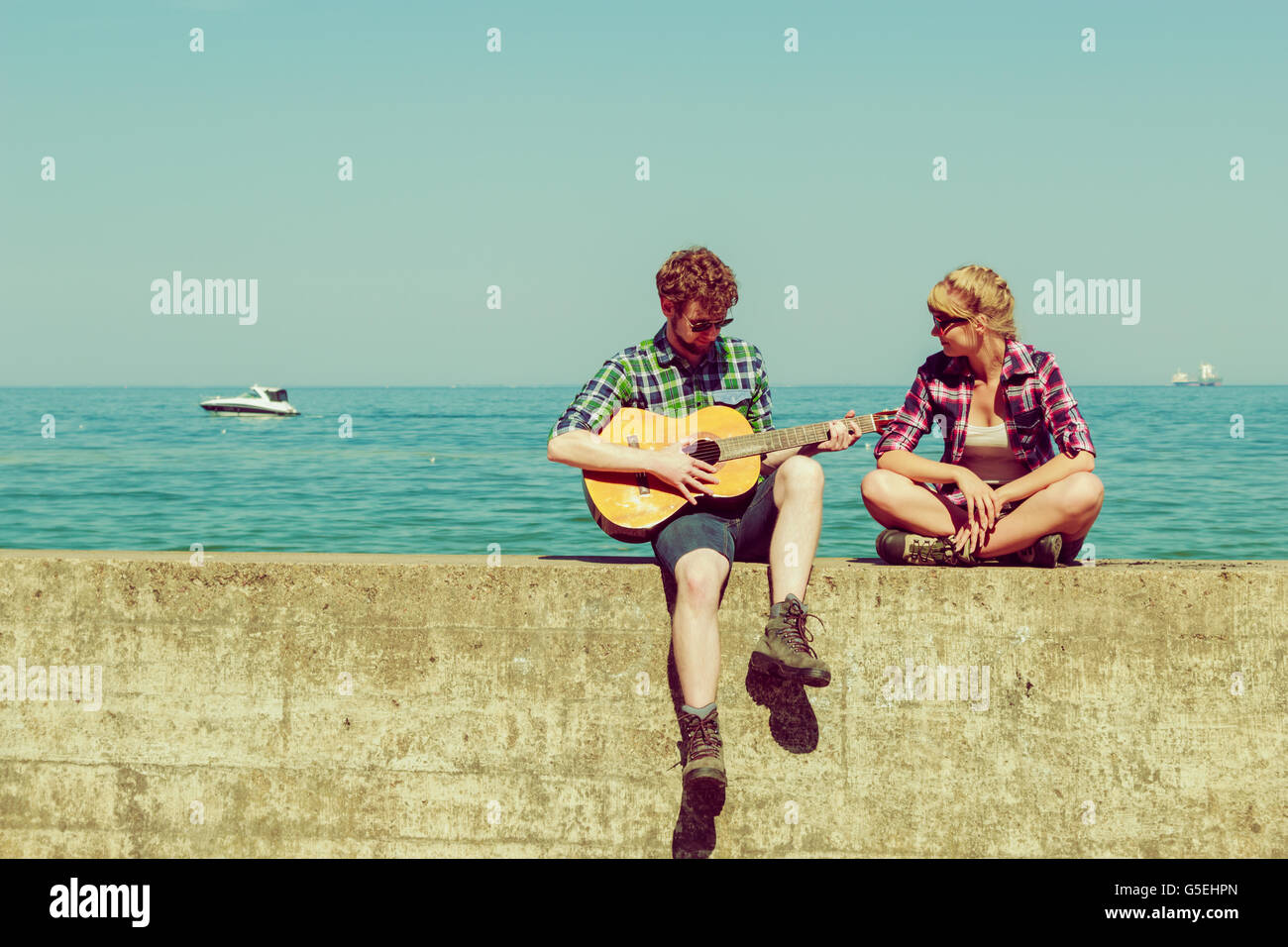 Young man playing guitar to his girlfriend outdoor sunny summer day by ...