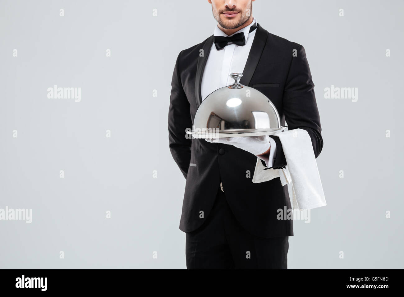 Closeup of butler in tuxedo and gloves holding silver tray with lid and ...