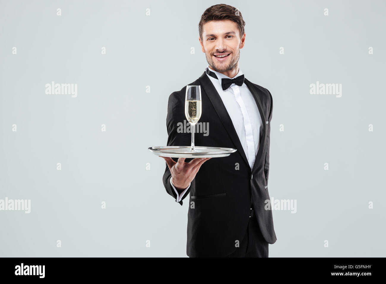 Cheerful young butler in tuxedo with bow tie standing and offering you ...
