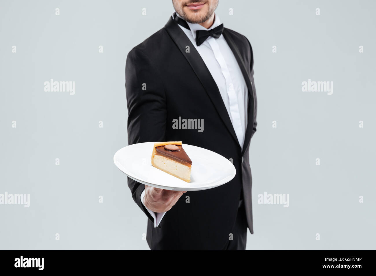 Butler in tuxedo with bowtie holding plate with piece of cake Stock ...