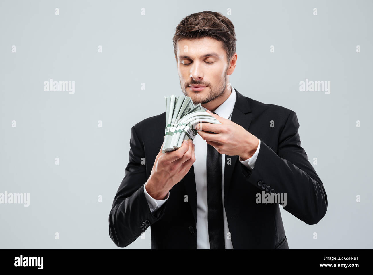 Handsome young businessman holding and smelling money over white ...
